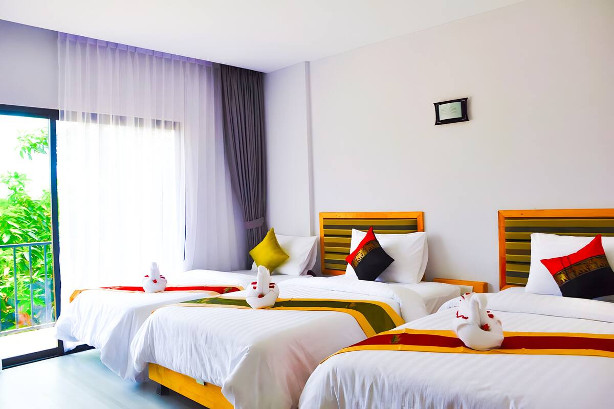 Quarto de hotel com três camas, varanda e vista para o verde.