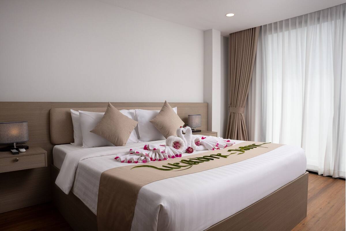 Cama bem arrumada com tapete de boas-vindas, almofadas e toalhas decorativas em formato de cisne.