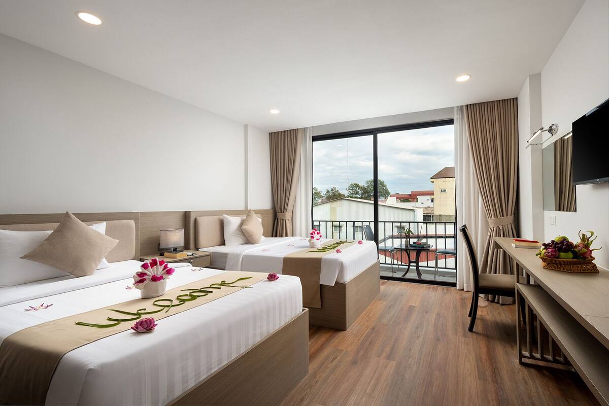 Quarto de hotel com duas camas, uma mesa e varanda com vista.