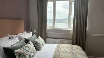 Quarto de hotel com cama, janela com cortinas e vista para o mar.