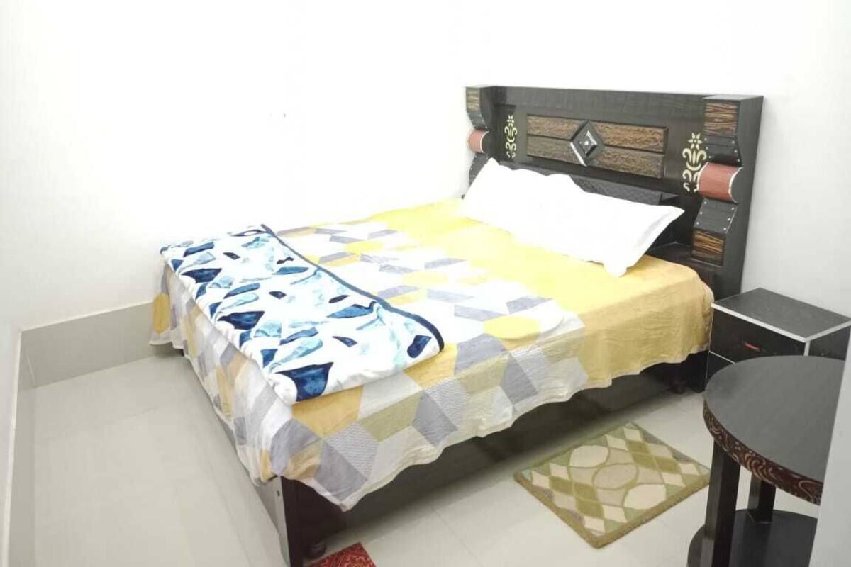 Uma cama com colcha estampada, uma mesa de cabeceira e uma pequena mesa redonda.