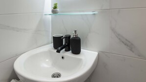 Um banheiro com pia de mármore branco, espelho redondo com iluminação e uma pequena prateleira com uma planta.