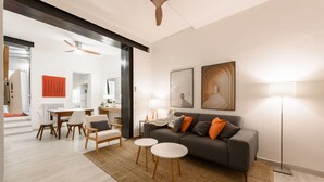 Uma sala de estar moderna com um sofá cinzento, duas mesas redondas e um espaço de jantar com uma mesa e cadeiras brancas.