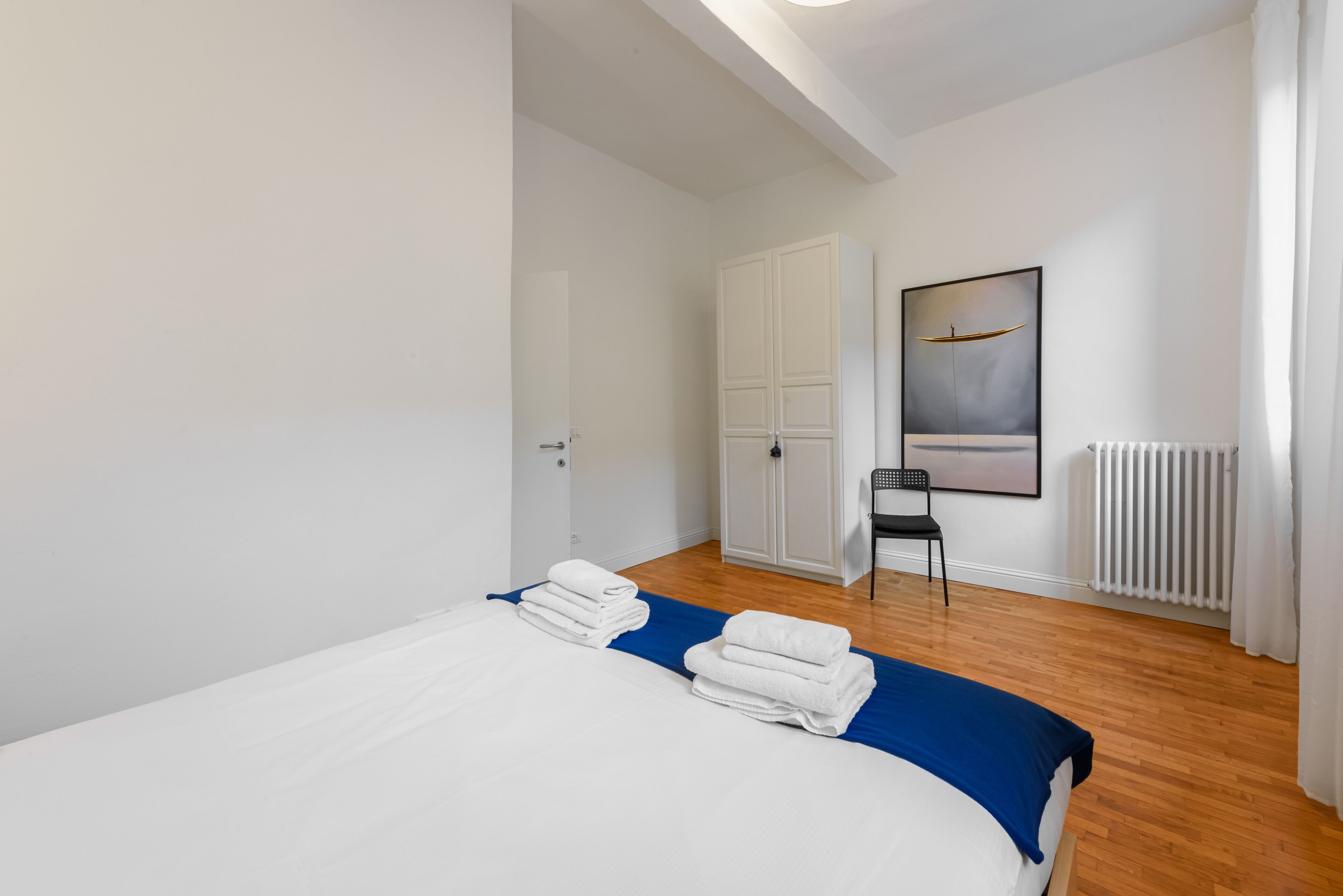 Quarto de hotel com cama, cadeira, guarda-roupa e radiador.