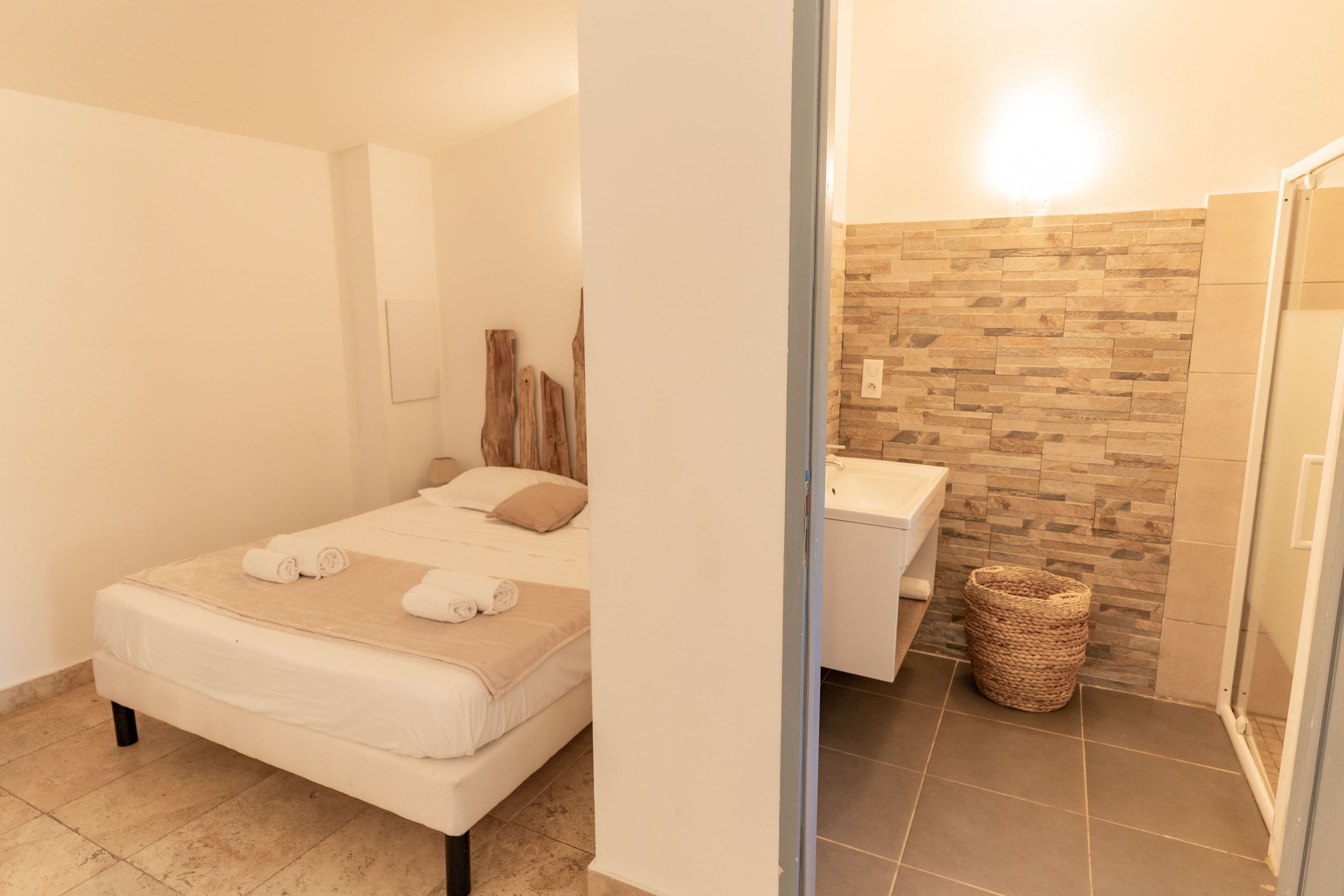 Quarto de hotel com uma cama, banheiro com pia e chuveiro.