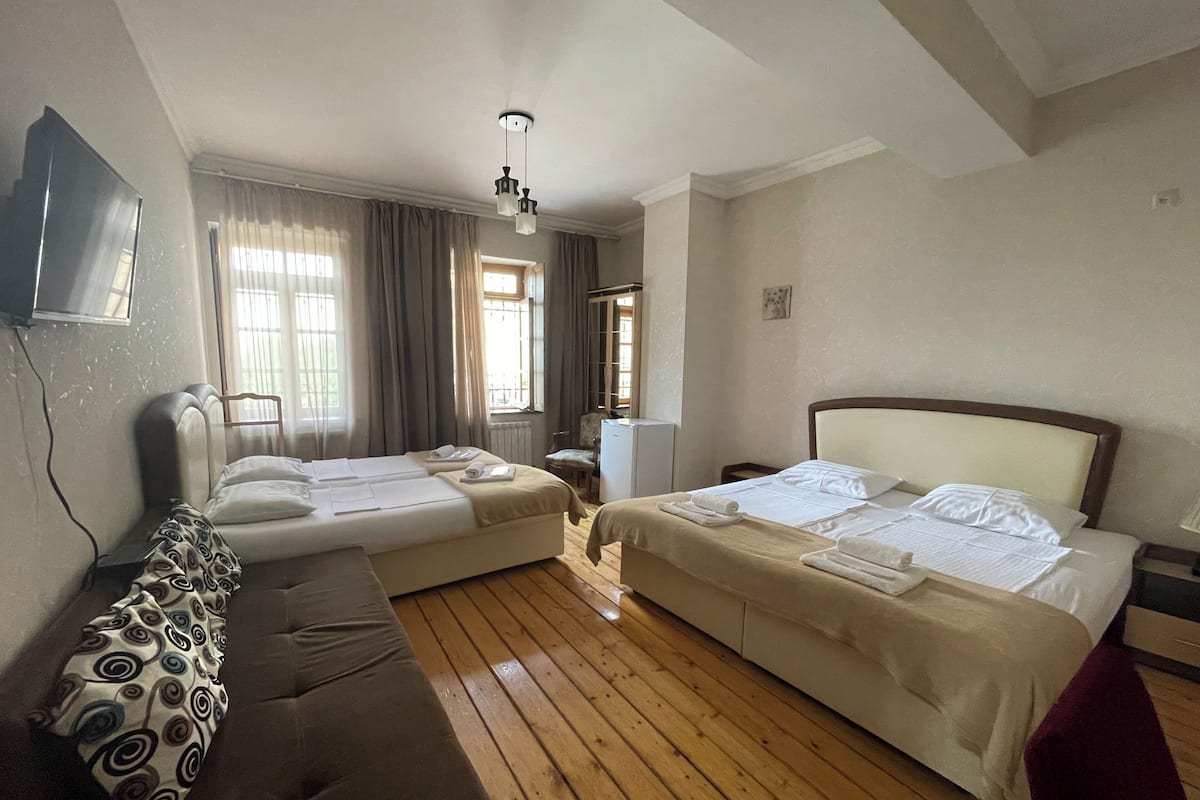 Quarto de hotel com duas camas, um sofá, uma TV e uma janela com cortinas.