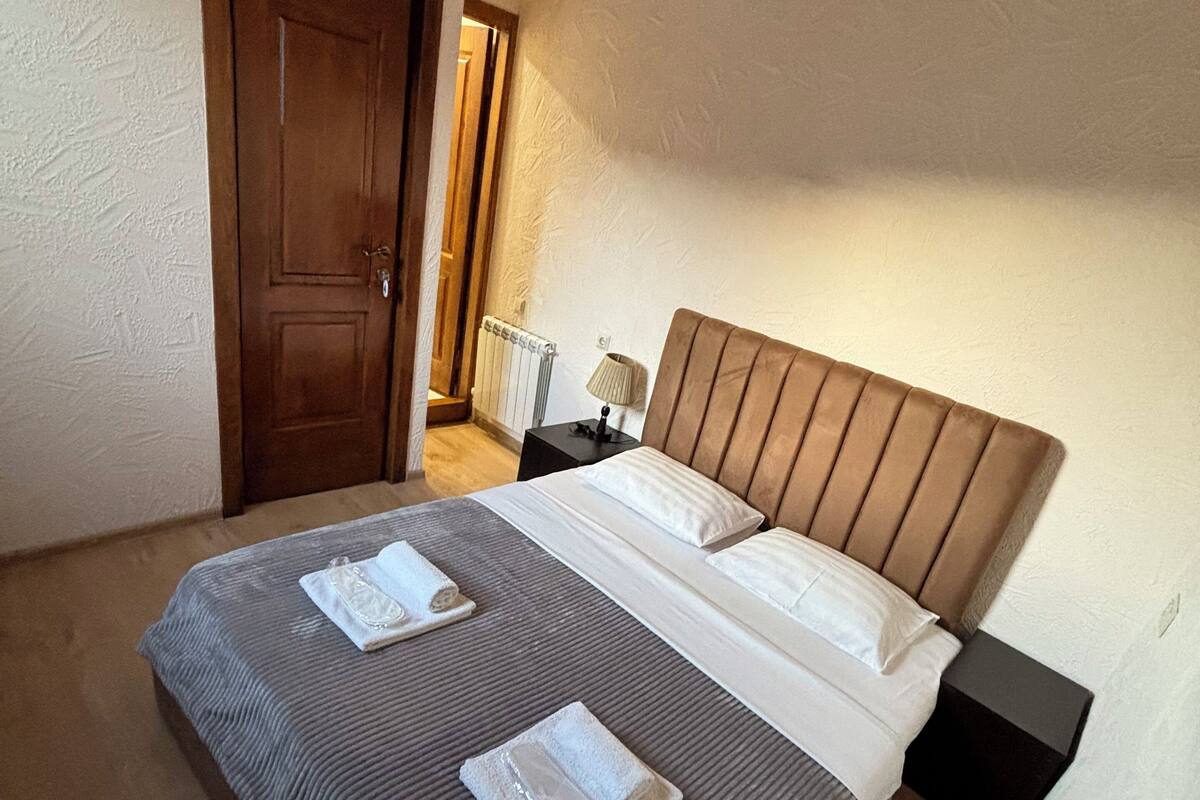 Quarto de hotel com cama, porta de madeira, radiador, abajur e unidade de ar condicionado.