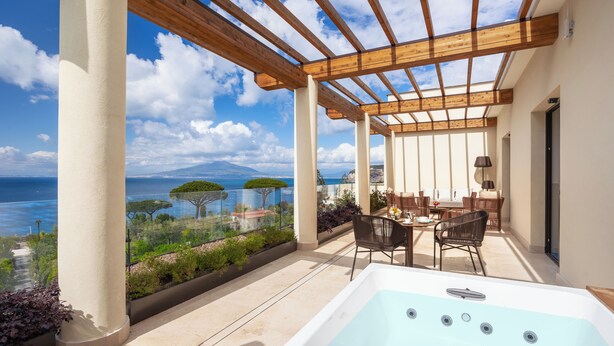 Uma varanda com pérgola de madeira, banheira de hidromassagem e área de refeições com cadeiras e mesa.