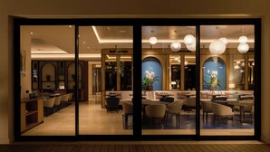 Um hall de hotel moderno com área de estar ampla, grandes janelas e luminárias contemporâneas.