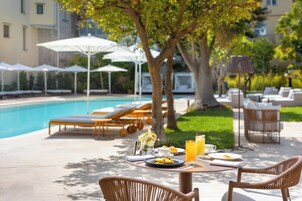 Área de refeições à beira da piscina com espreguiçadeiras, guarda-sóis e uma mesa posta para o café da manhã.
