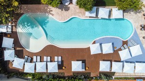 Vista aérea de uma piscina com espreguiçadeiras e guarda-sóis, cercada por um deck de madeira e vegetação.