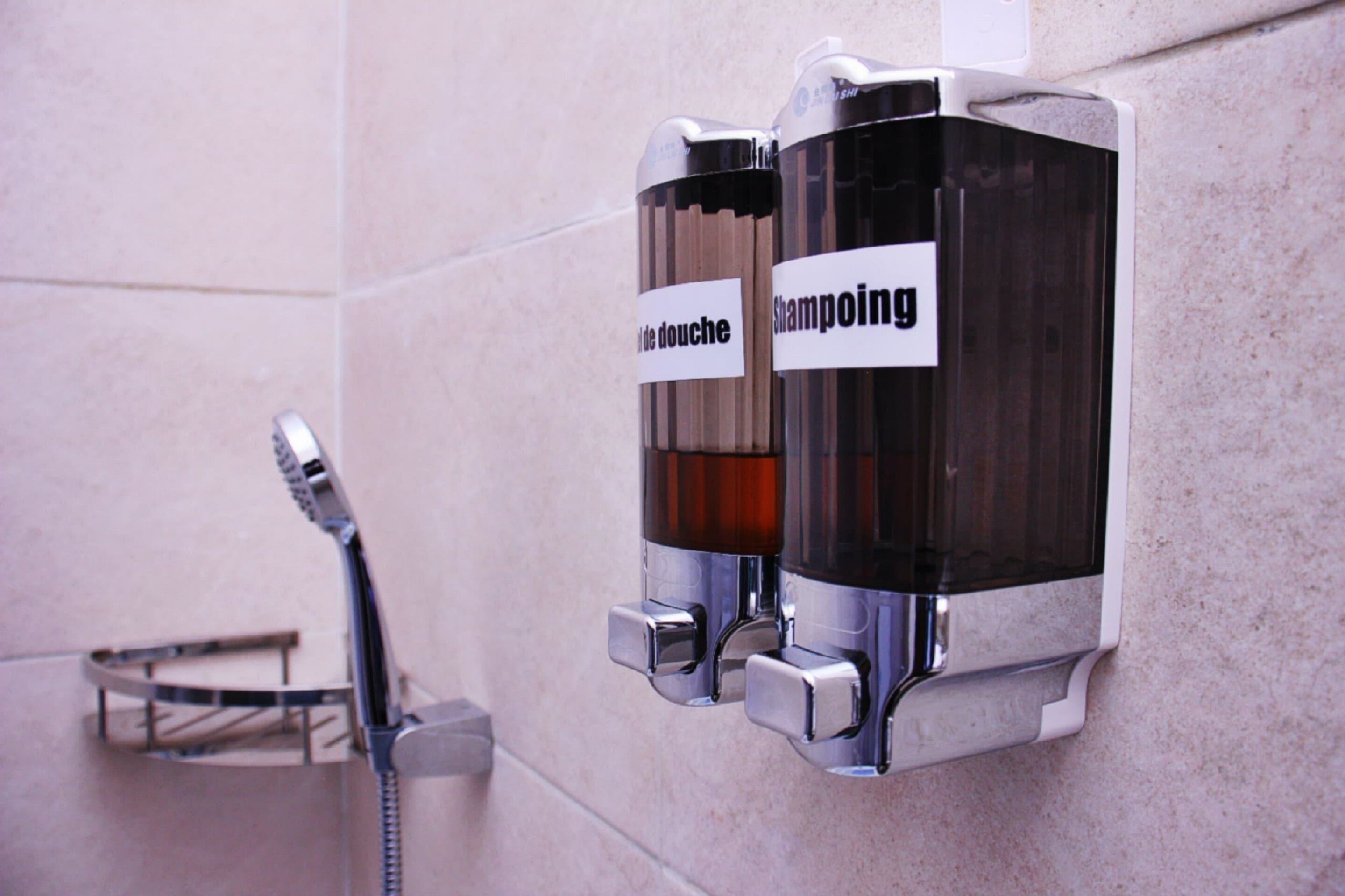 Um chuveiro fixado na parede, com dois frascos identificados como 'shampoo' e 'shampooing'.