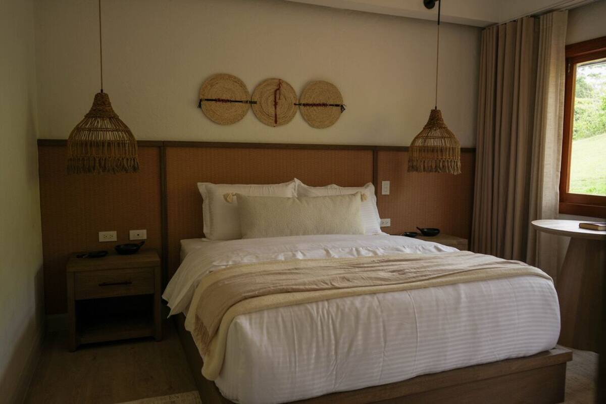 Quarto com uma cama grande, duas mesas de cabeceira, uma mesa redonda e três obras de arte na parede.
