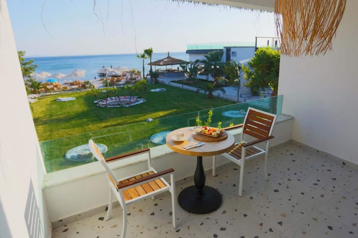 Varanda com vista para a praia e área da piscina, mobiliada com mesa e duas cadeiras.