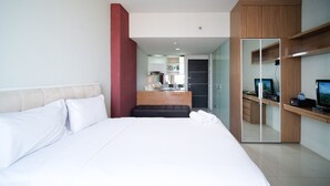 Quarto de hotel moderno com uma cama grande, um pequeno espaço de estar, uma kitchenette e uma televisão.