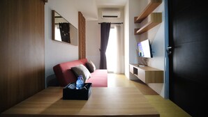 Quarto de hotel com uma secretária de madeira, um sofá vermelho, uma TV em um suporte e uma janela com cortinas.