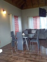 Uma área de refeições com mesa e cadeiras de vidro, um sofá e cortinas com padrão de bolinhas.