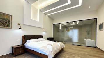 Quarto de hotel moderno com uma cama grande, mesas de cabeceira, um criado-mudo, uma luminária na parede e uma janela ampla.