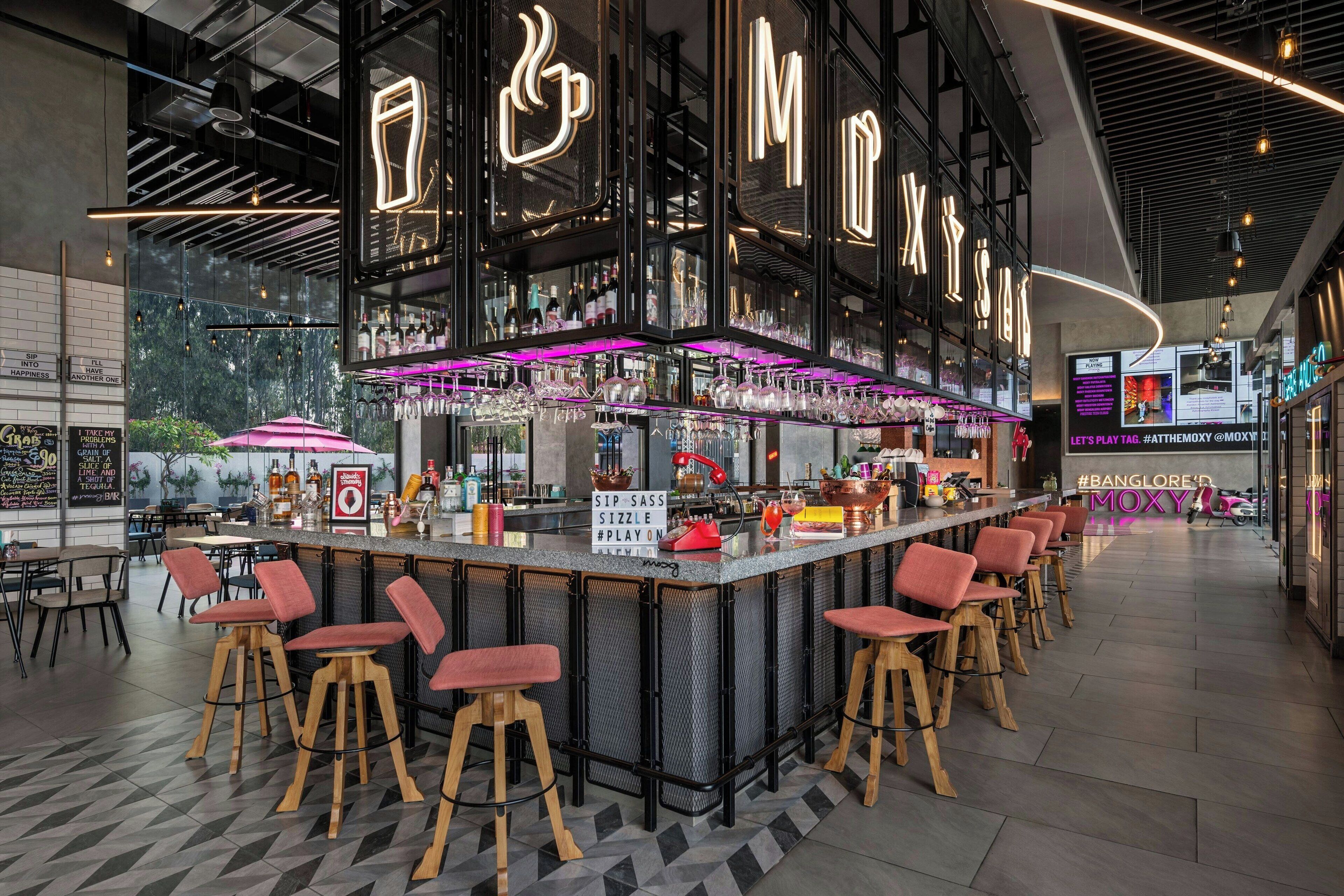 Uma área de bar moderna com balcão, banquetas e letreiros de neon.