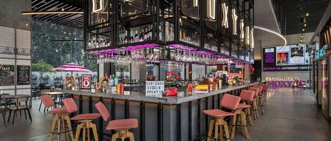Uma área de bar moderna com balcão, banquetas e letreiros de neon.