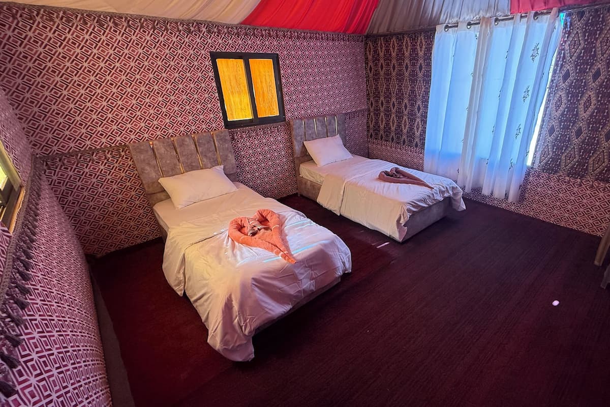 Quarto com duas camas, paredes estampadas, janela com cortinas e uma cadeira pequena.