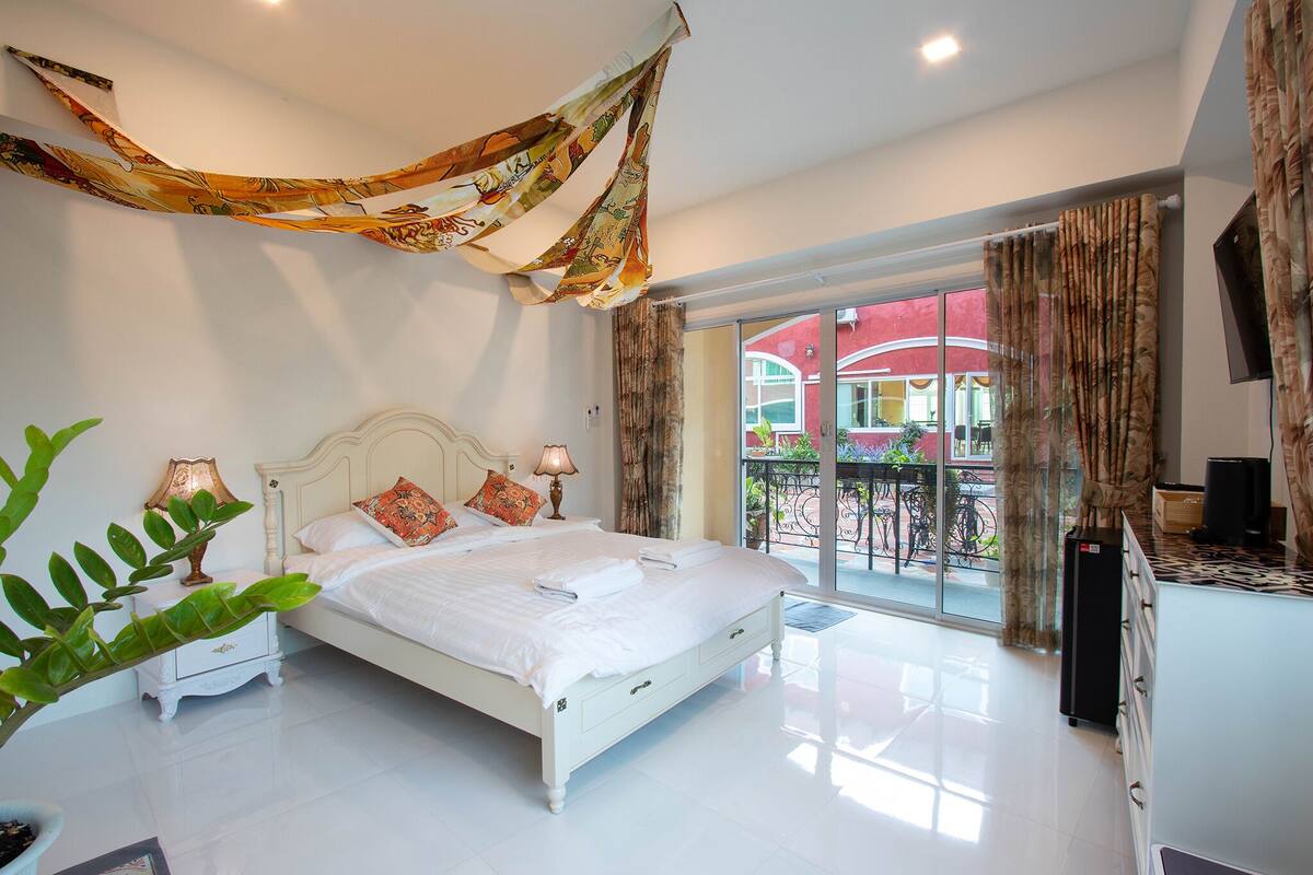 Um quarto amplo com uma cama grande, uma mesa de cabeceira, uma luminária e vista para a varanda.