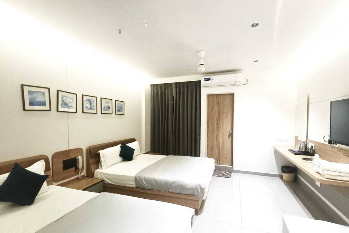 Quarto de hotel com duas camas, uma mesa, uma televisão e uma porta que dá para um banheiro.