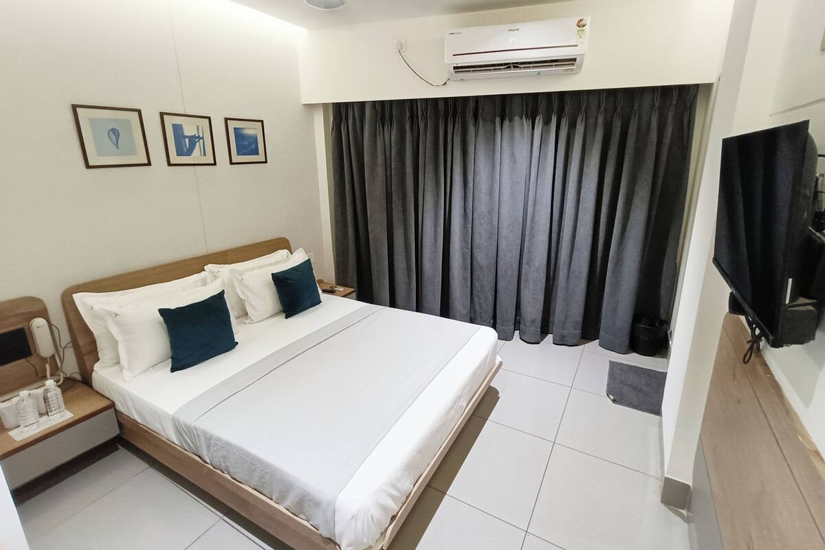Quarto de hotel com cama, mesa de cabeceira, ar condicionado, televisão e cortina.