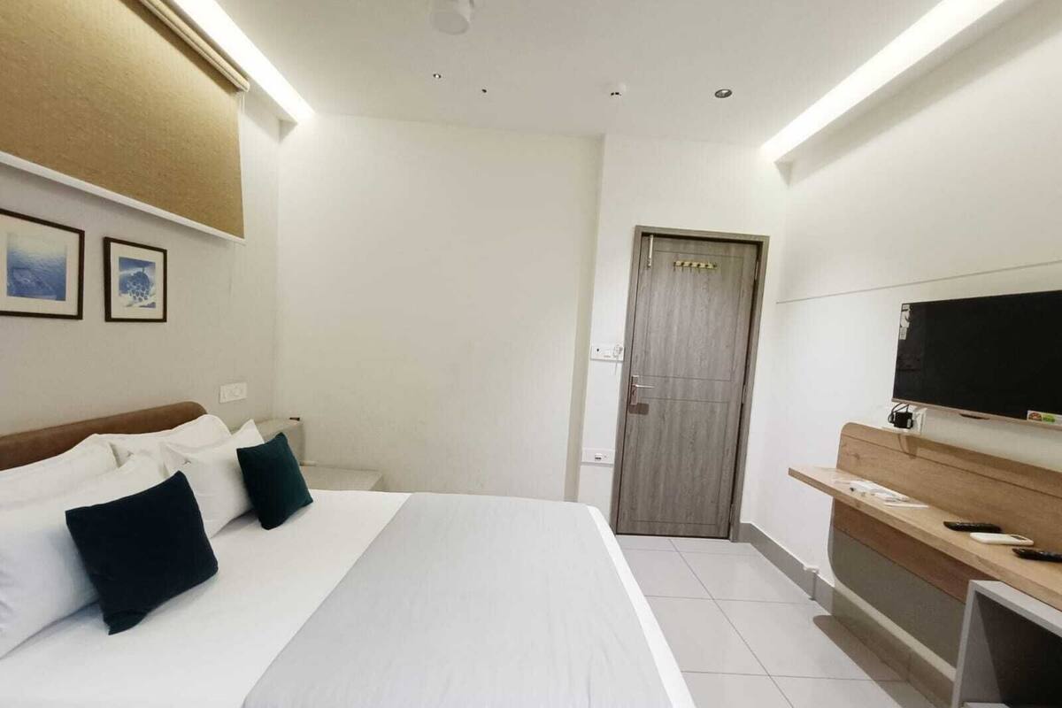 Quarto de hotel com uma cama grande, uma escrivaninha e uma televisão de tela plana, e uma porta.
