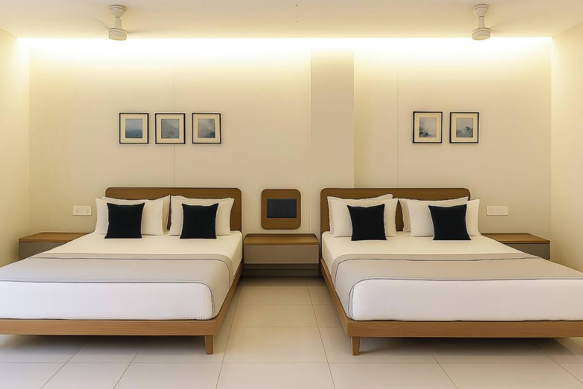 Quarto de hotel com duas camas, cada uma com cabeceira de madeira, roupa de cama branca e almofadas pretas. Há quadros emoldurados na parede acima de cada cama.