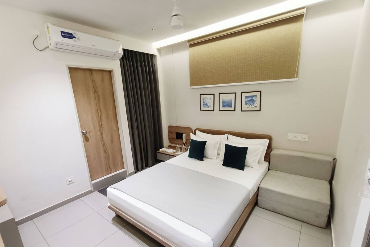 Quarto de hotel com cama, mesa de cabeceira e um pequeno espaço para sentar.