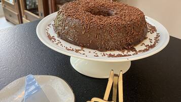 Um bolo bundt de chocolate sobre um prato branco, com raspas de chocolate, um garfo para bolo e uma placa com a inscrição 'BRIGADE 1'.