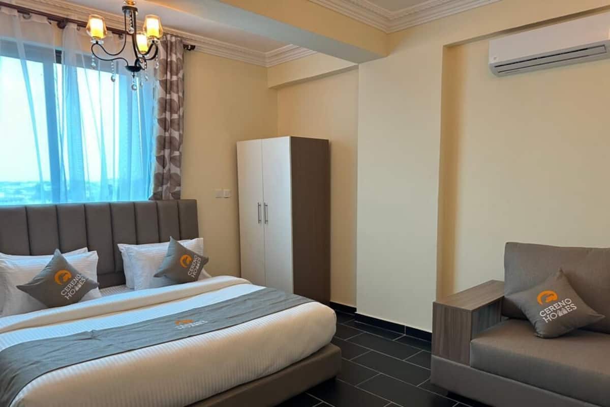 Quarto de hotel com uma cama grande, um sofá, um guarda-roupa e uma janela com cortinas.