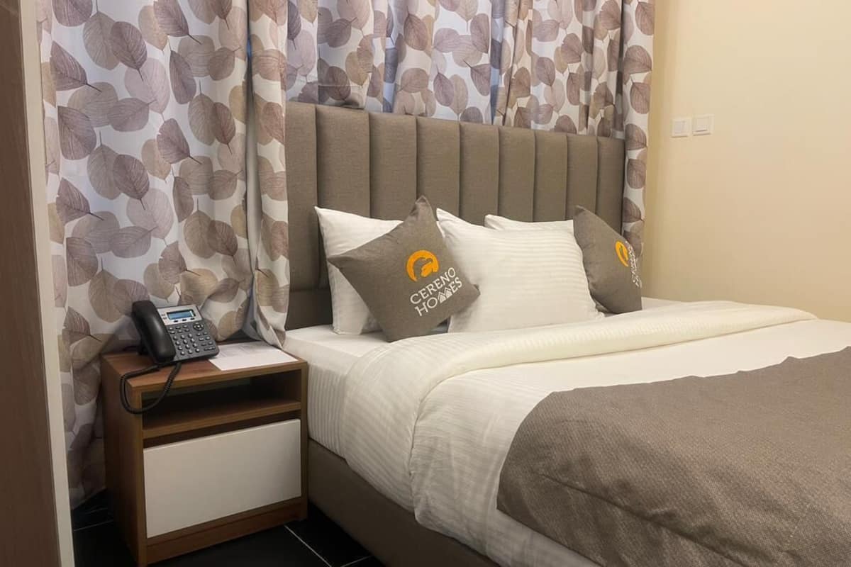 Quarto de hotel com uma cama, uma mesa de cabeceira com telefone e cortinas com padrão de folhas.