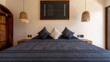 Quarto com uma cama grande, duas luminárias pendentes, uma obra de arte emoldurada na parede e uma porta de madeira.
