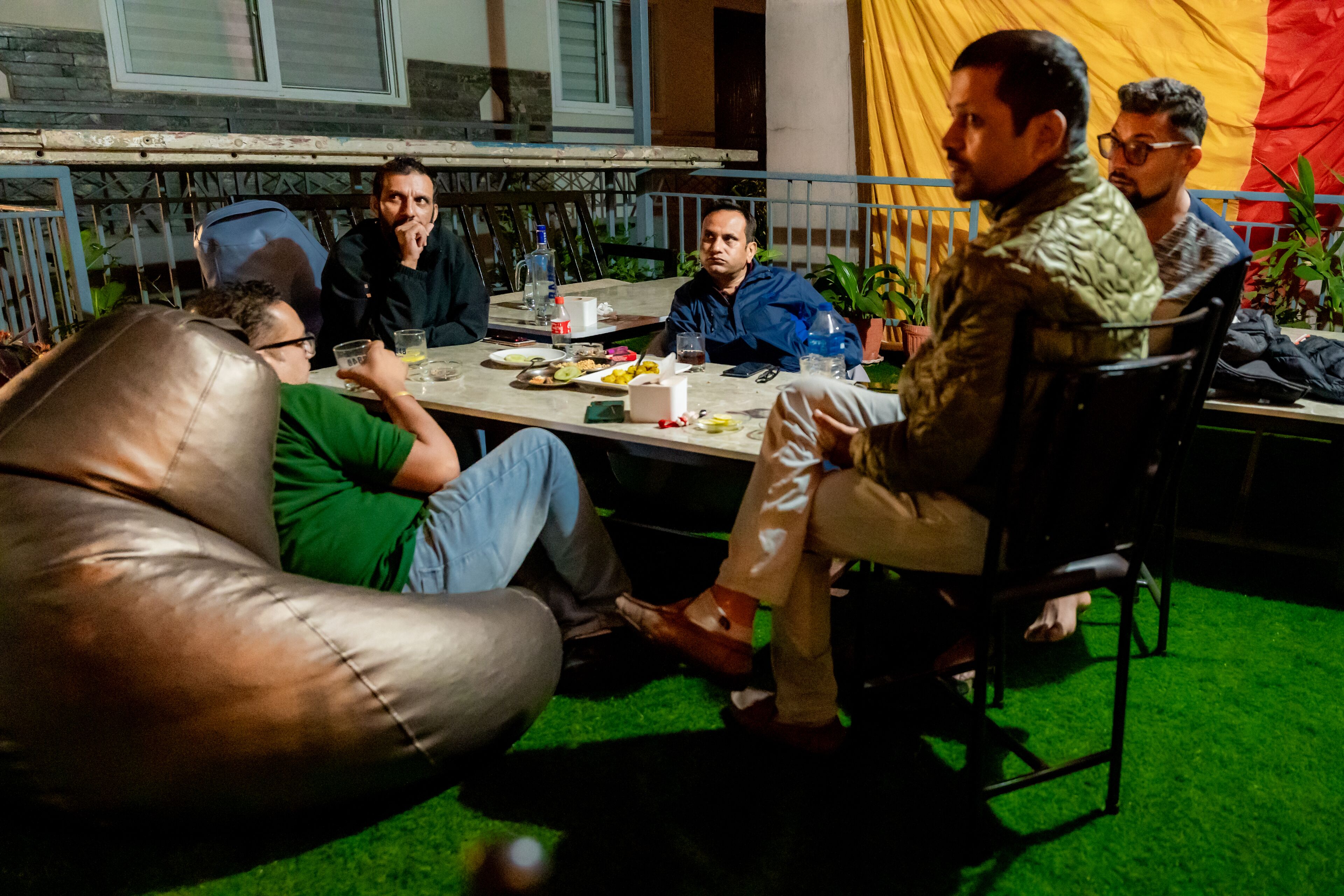 Um grupo de pessoas sentado à volta de uma mesa em um quarto com carpete verde, uma janela e uma cortina.