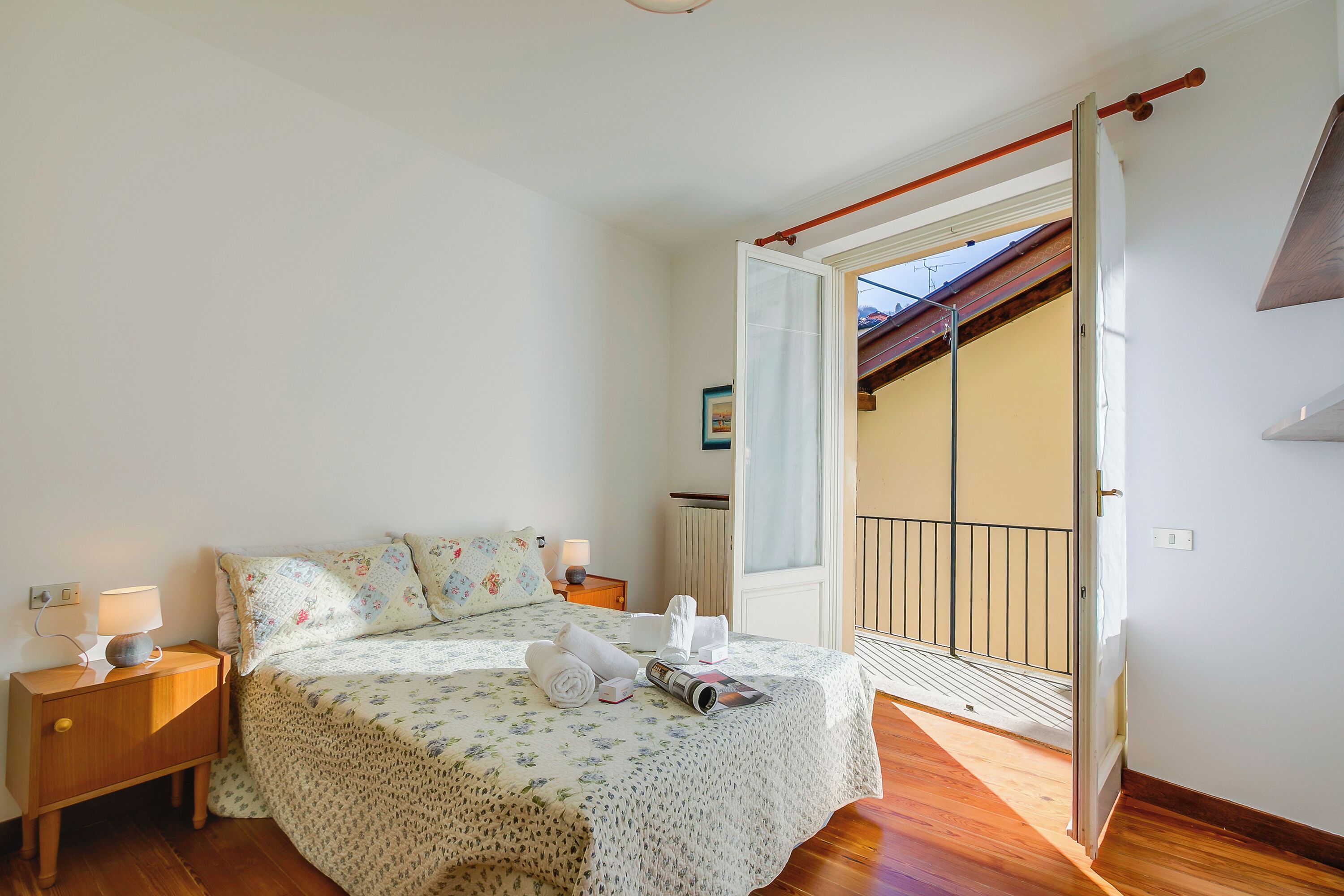 Quarto com cama, mesa de cabeceira e porta que dá para uma varanda.