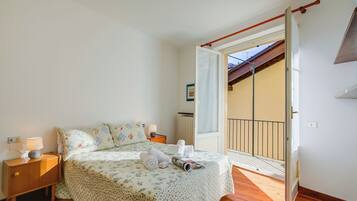 Quarto com cama, mesa de cabeceira e porta que dá para uma varanda.