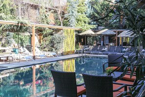 Área de piscina com espreguiçadeiras, deck de madeira e uma cascata.