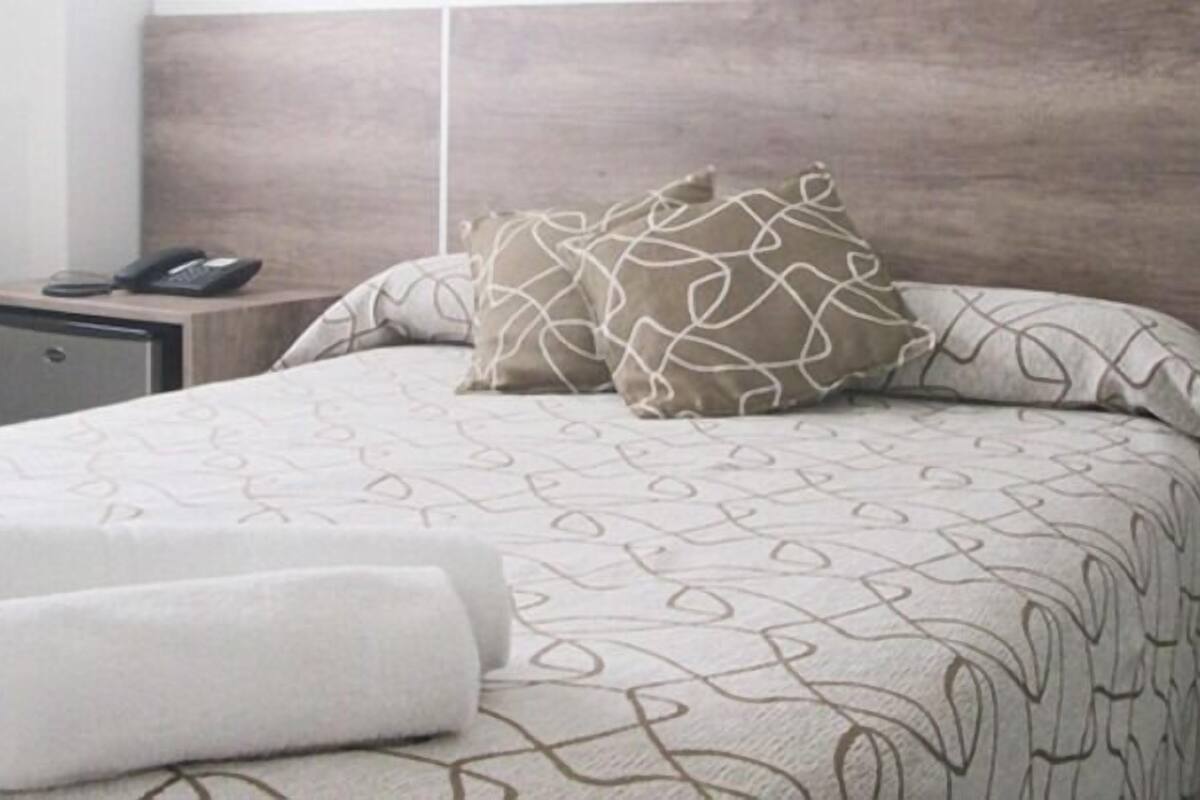 Cama bem arrumada com roupa de cama estampada, mesa de cabeceira com telefone e criado-mudo.