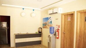Quarto de hotel com cozinha compacta, dispensador de água, extintor de incêndio e porta com aviso.