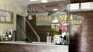 Uma mesa de recepção com acabamento em madeira, uma divisória de vidro e uma placa com a inscrição "MALANI HOSTERIA".