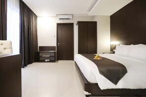 Quarto de hotel com cama, escrivaninha, guarda-roupa e ar condicionado.