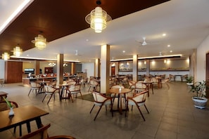Um restaurante espaçoso com várias mesas e cadeiras, ventiladores de teto e iluminação pendente.