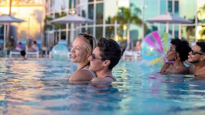Área de piscina com água cristalina, um edifício moderno com grandes janelas e um teto decorativo.