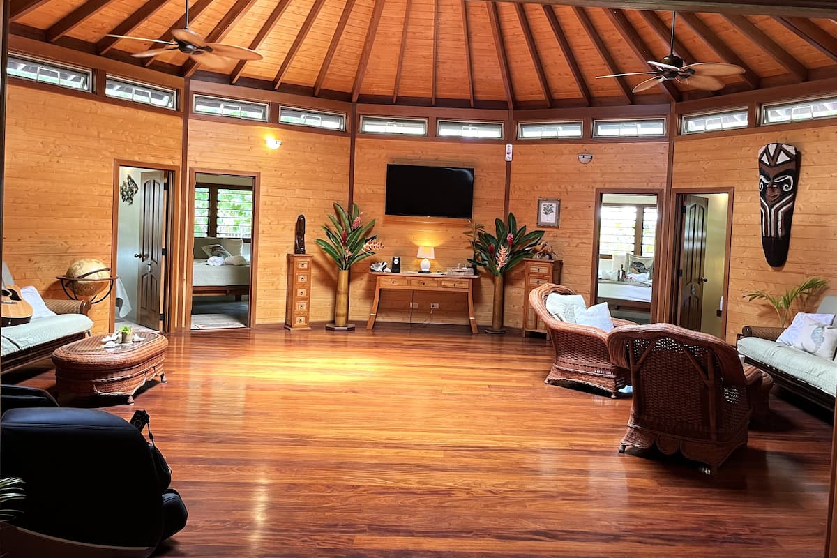 Uma sala de estar ampla com piso de madeira, ventilador de teto e TV de tela plana fixada na parede.