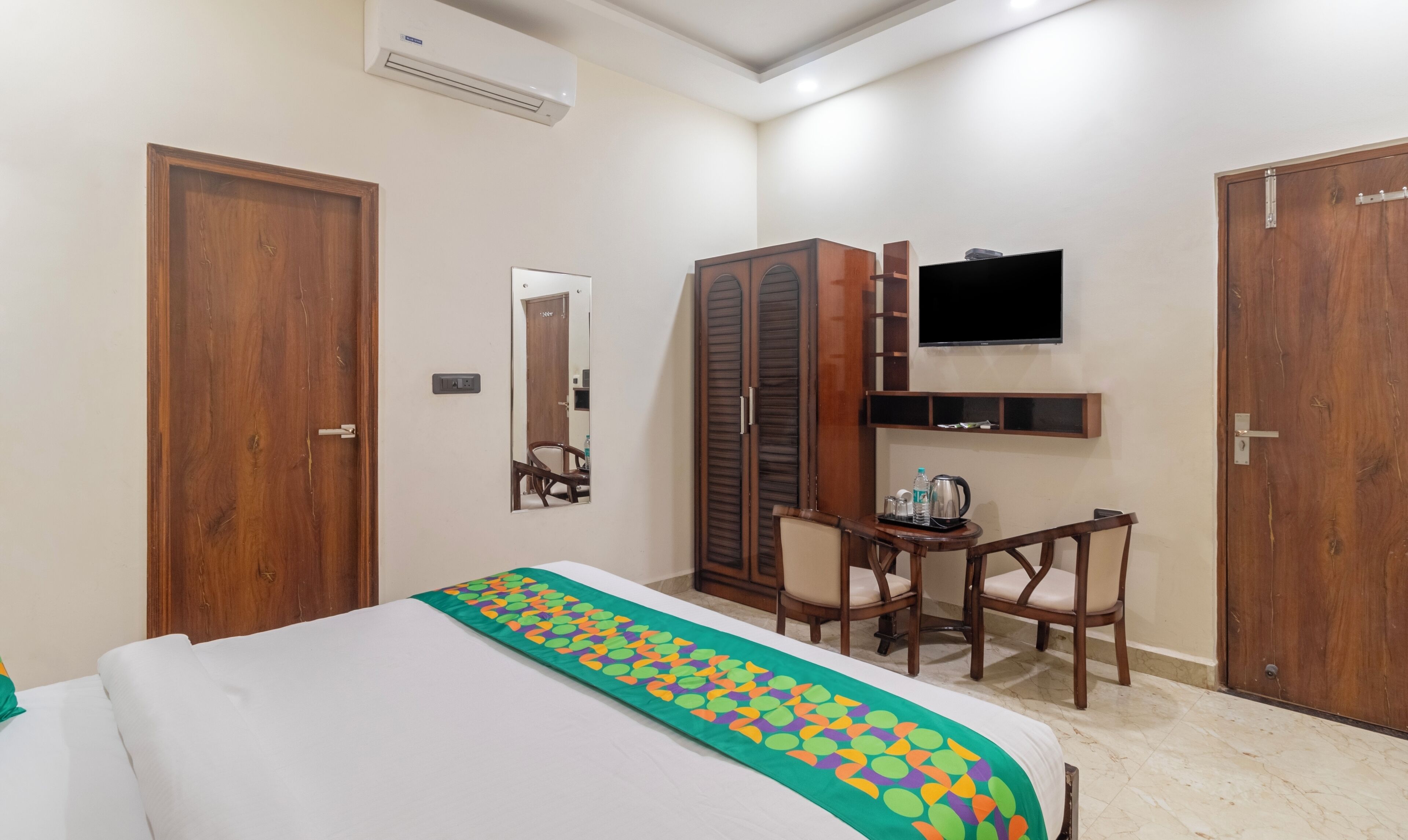 Quarto de hotel com cama, secretária com cadeiras, televisão e guarda-roupa.