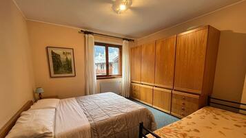 Quarto com cama, guarda-roupa, janela com cortinas e radiador.