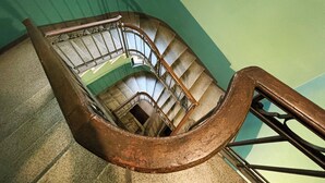 Uma escadaria em espiral com guarda-corpos de metal e degraus de madeira, que dá acesso a um andar superior.