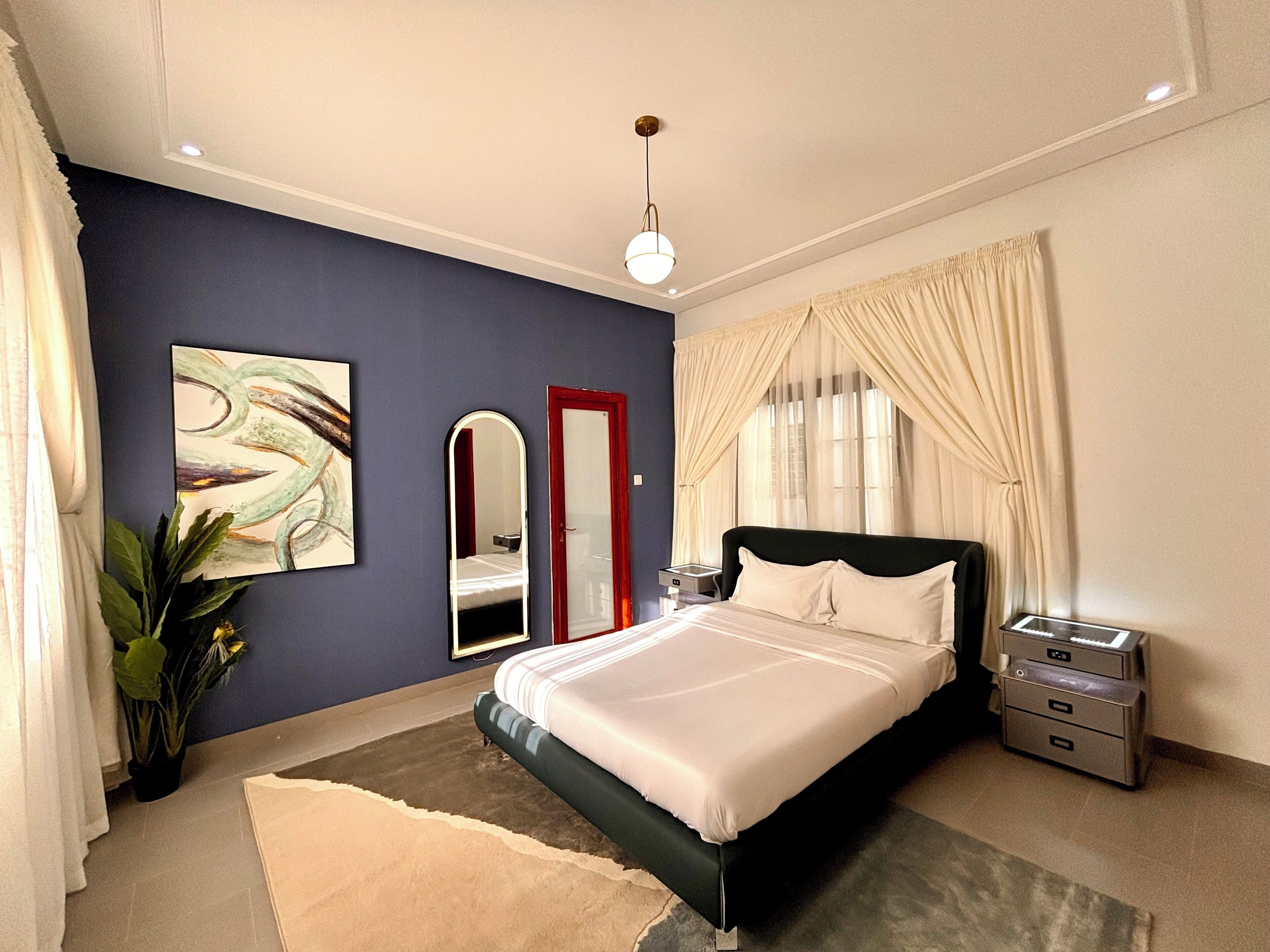 Quarto moderno com cama, mesas de cabeceira, espelho e planta em vaso.